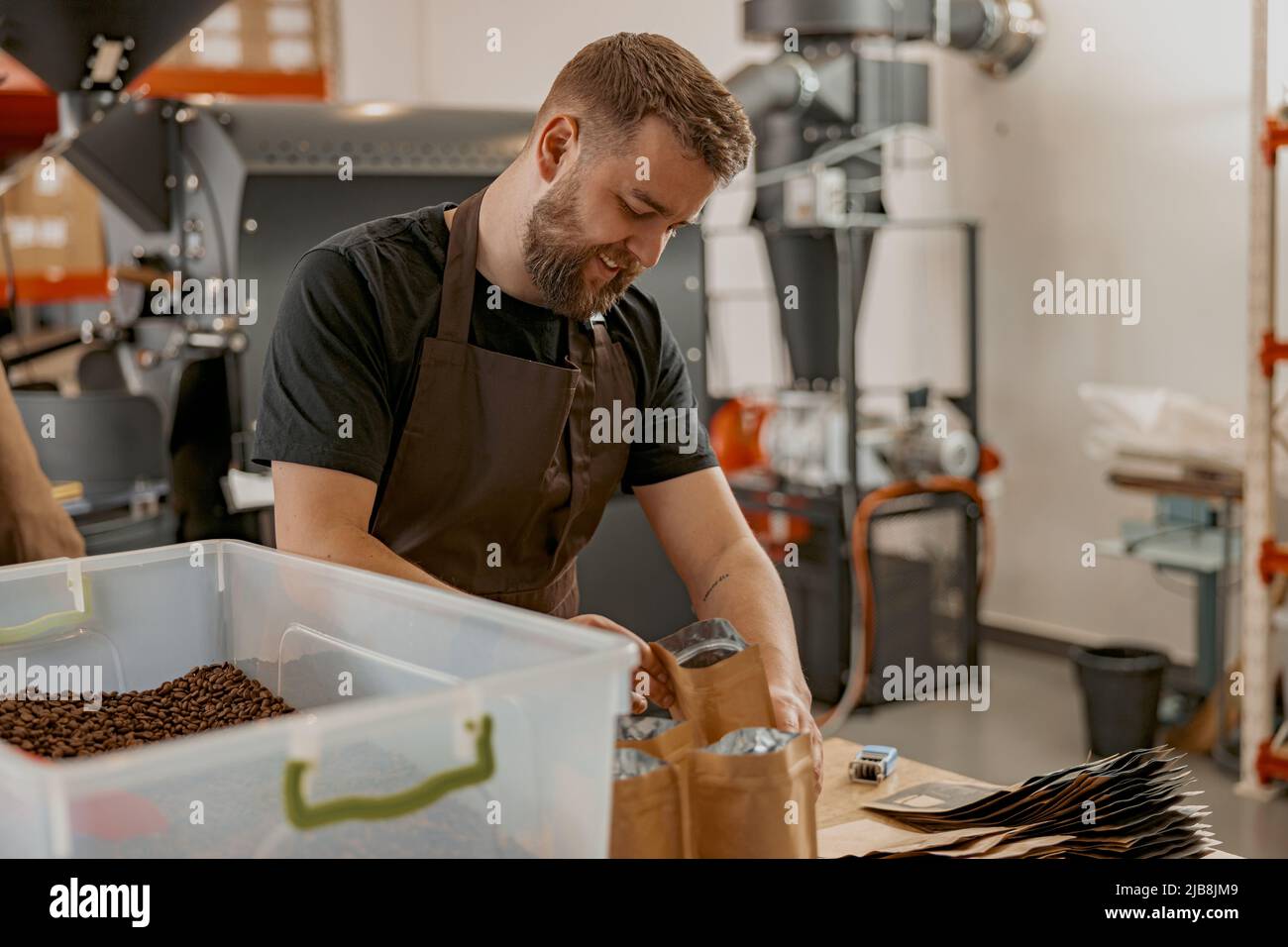 Business owner in uniform packs roasted coffee beans into packages for ...