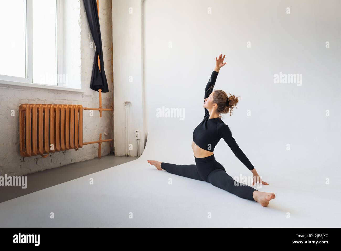 A young woman in black sportswear, stretches the muscles of the legs ...