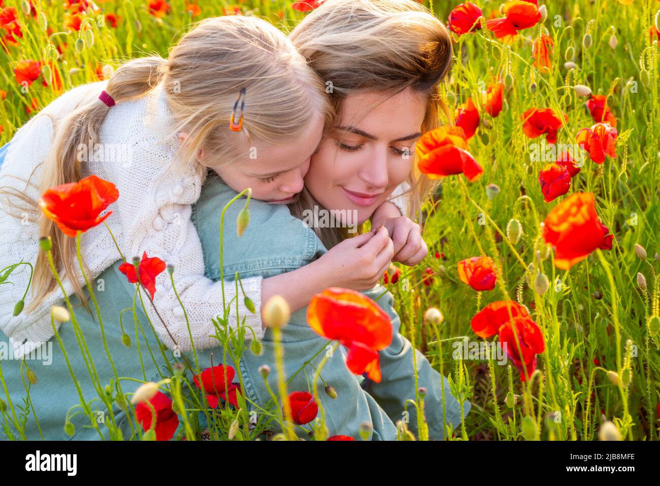 Portrait of mother and daughter walking through a flowering poppy field. Summer family holidays ...