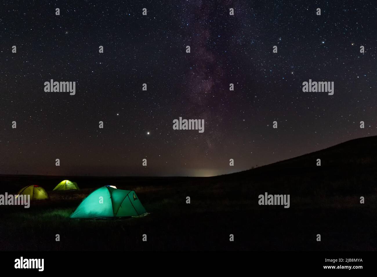 Travel and camping concept - three glowing camping tents at night under a starry sky with milky ...