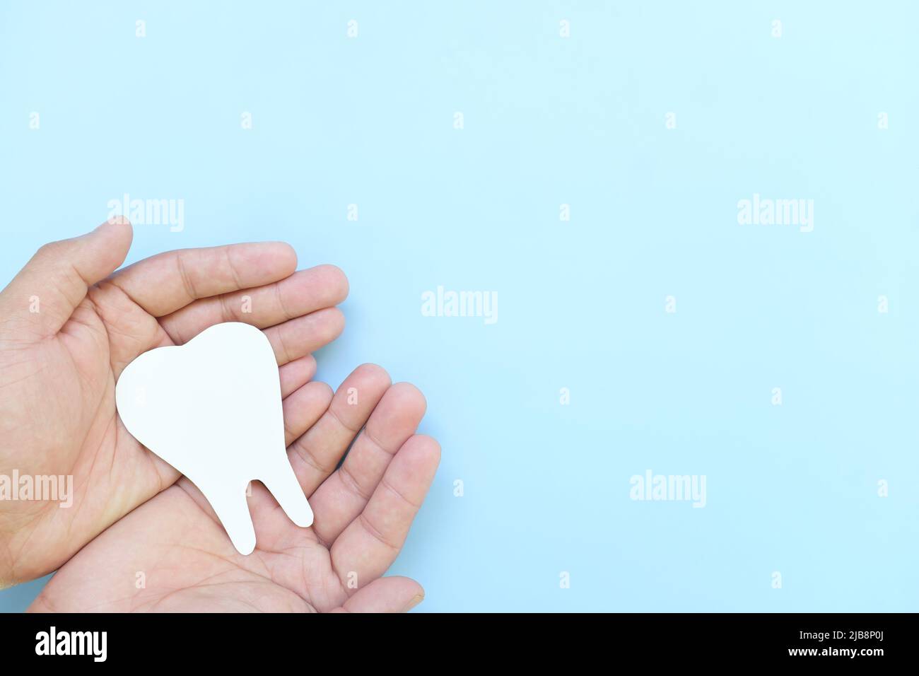 Top view of hands holding a big white tooth cutout in blue background ...