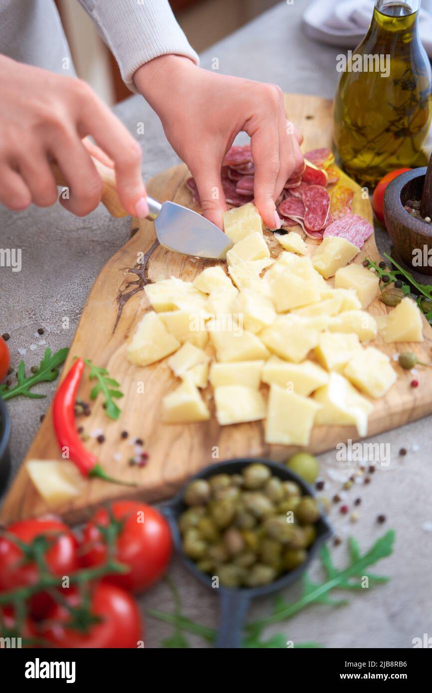Woman chopping Parmesan cheese with knife on grey table at domestic ...