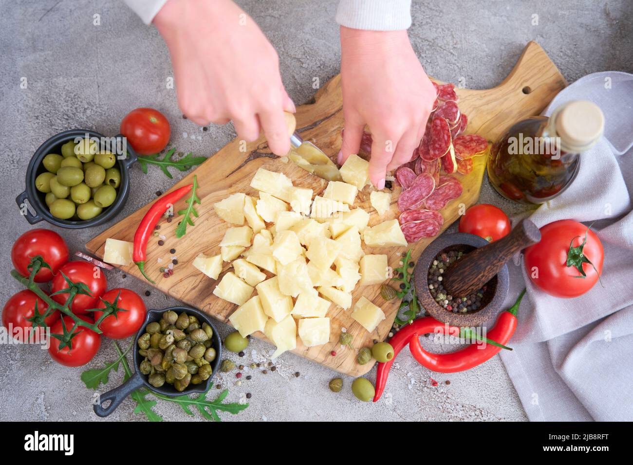 Woman chopping Parmesan cheese with knife on grey table at domestic ...