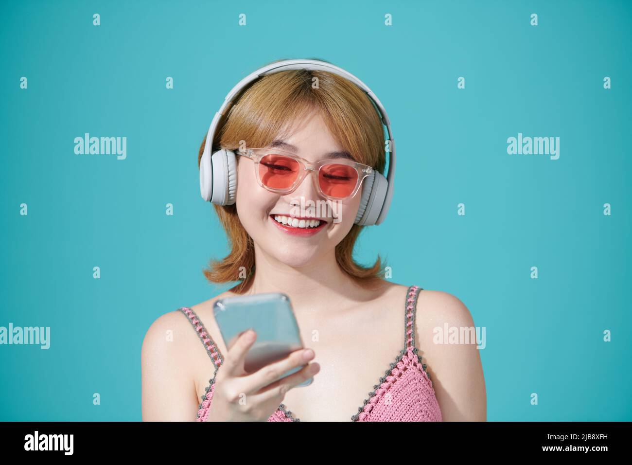 Happy cheerful Asian woman wearing wireless headphones listening to music from smartphone Stock ...