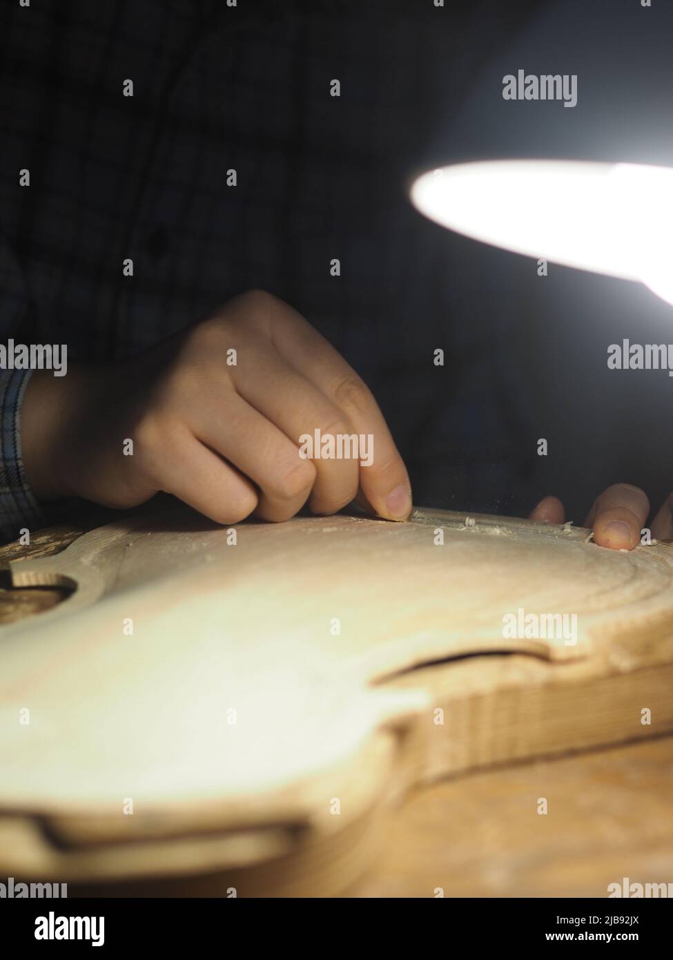 artisan working on raw wood violin plate with finger plane on the bench ...