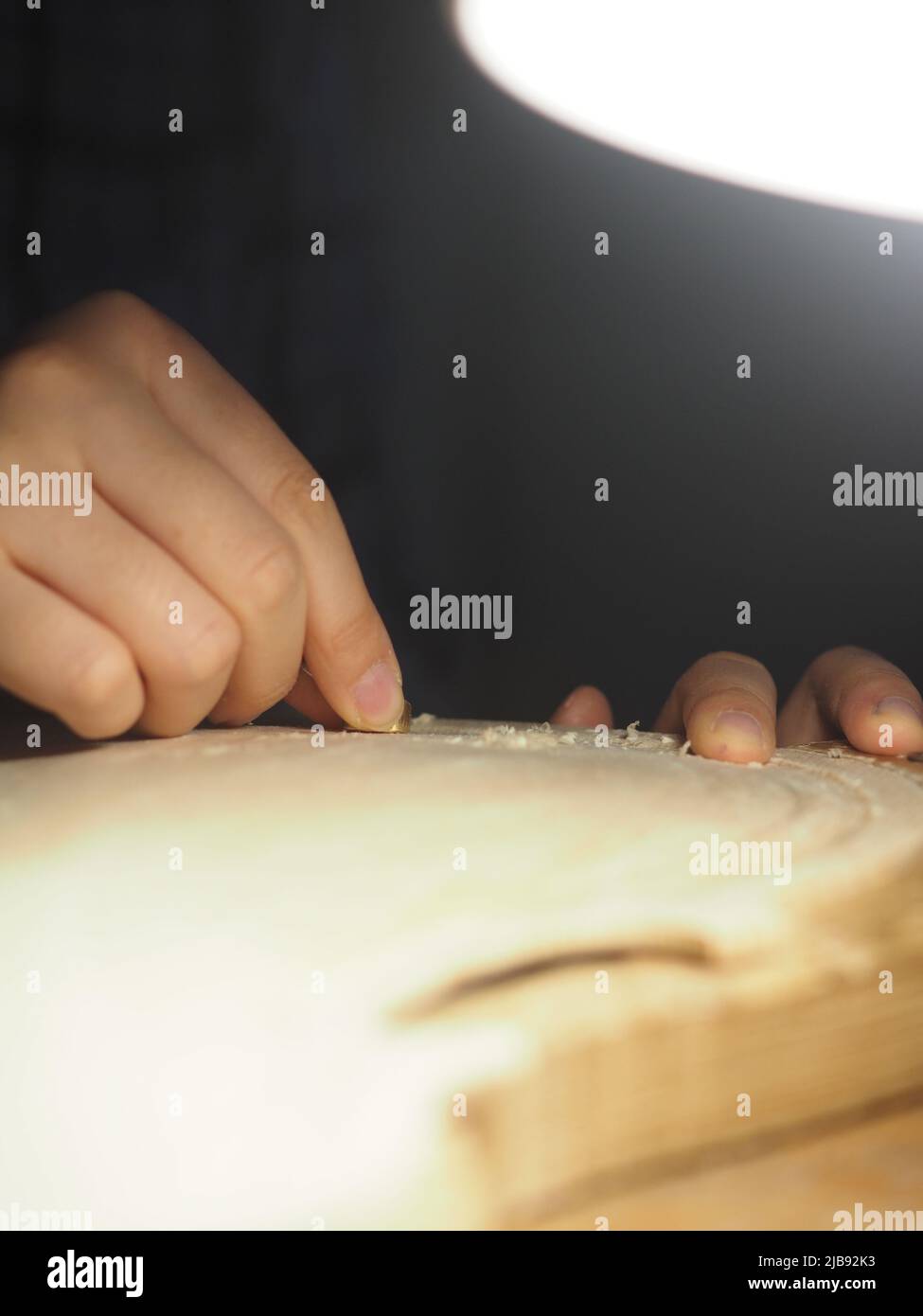 artisan working on raw wood violin plate with finger plane on the bench ...