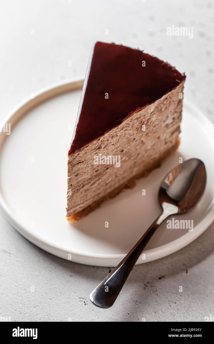 Chocolate cheesecake slice on a white plate with a spoon on white ...