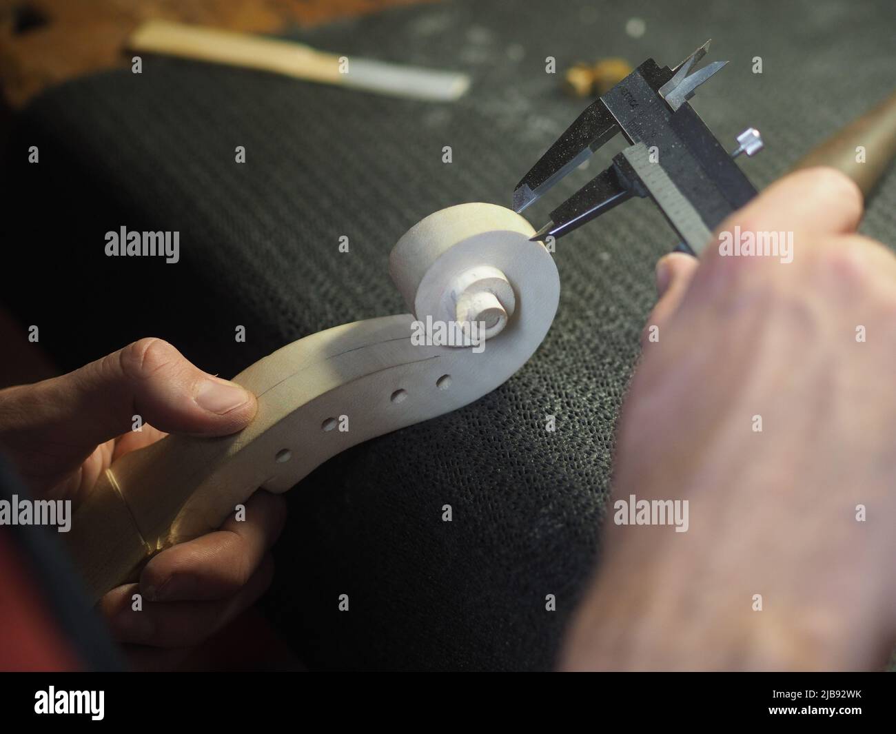 violin maker using a meter to shape and accurate measure fiddle scroll ...