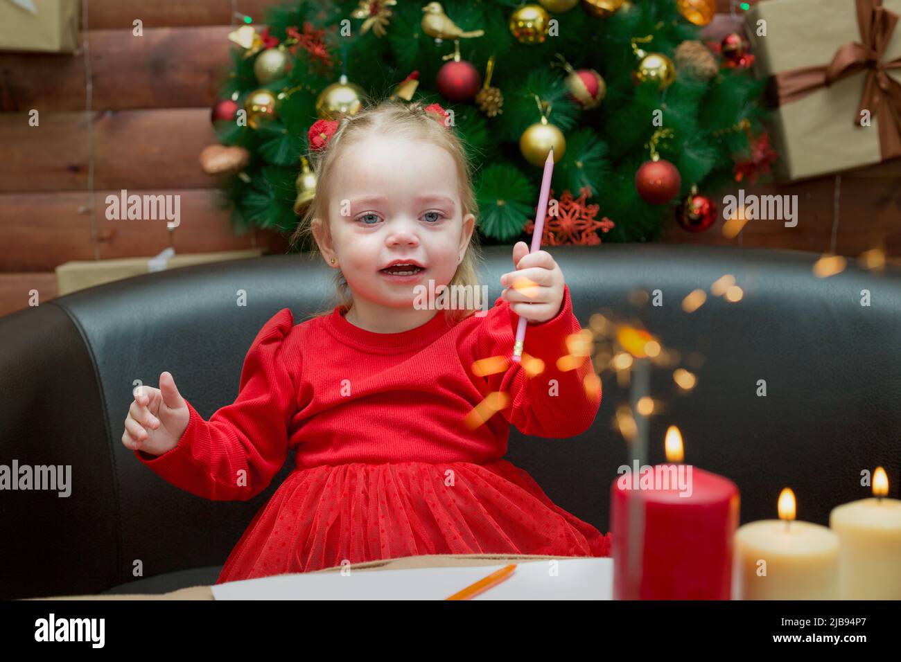 A little girl with a pencil in her hand looks lit firework sparkler ...