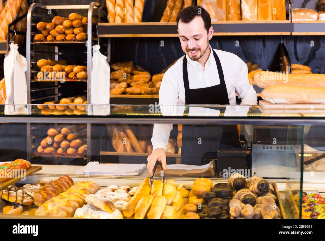 Male Shop Assistant Demonstrating Fresh Delicious Pastry In Bakery