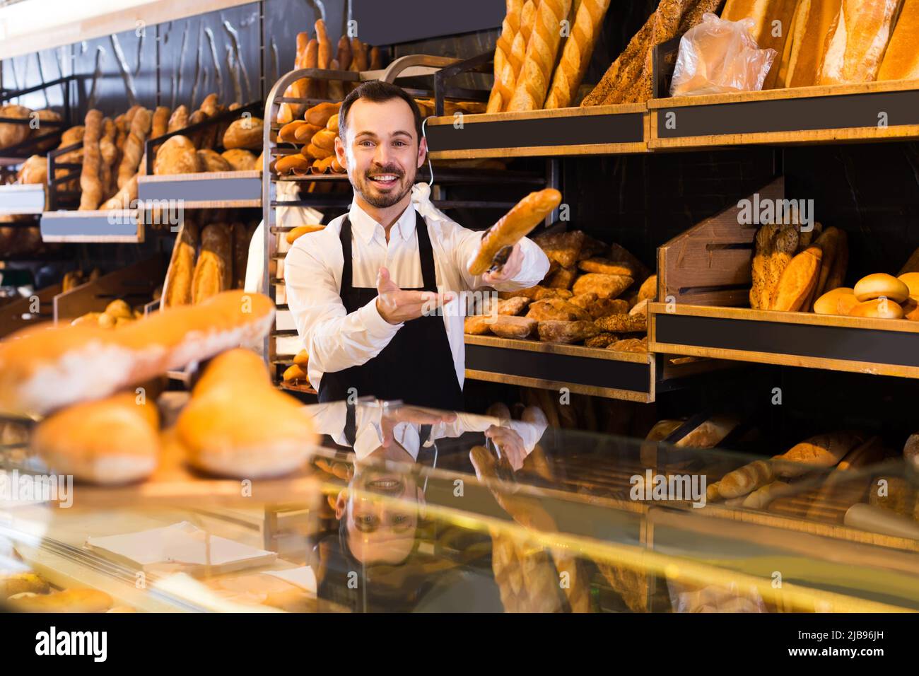 Male shop assistant demonstrating delicious loaves of bread in bakery ...