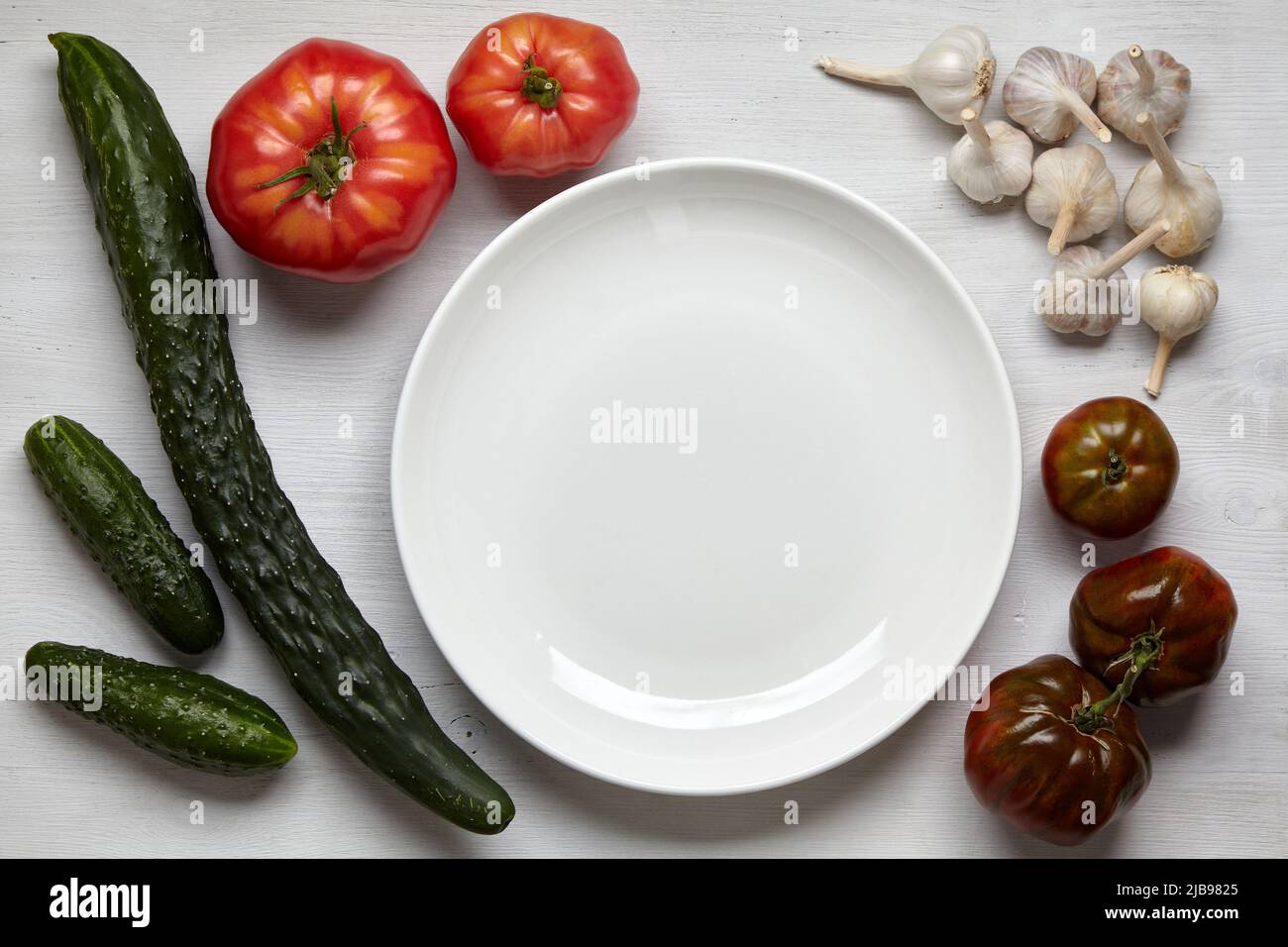A frame of homegrown vegetables on a wooden table with a white plate ...