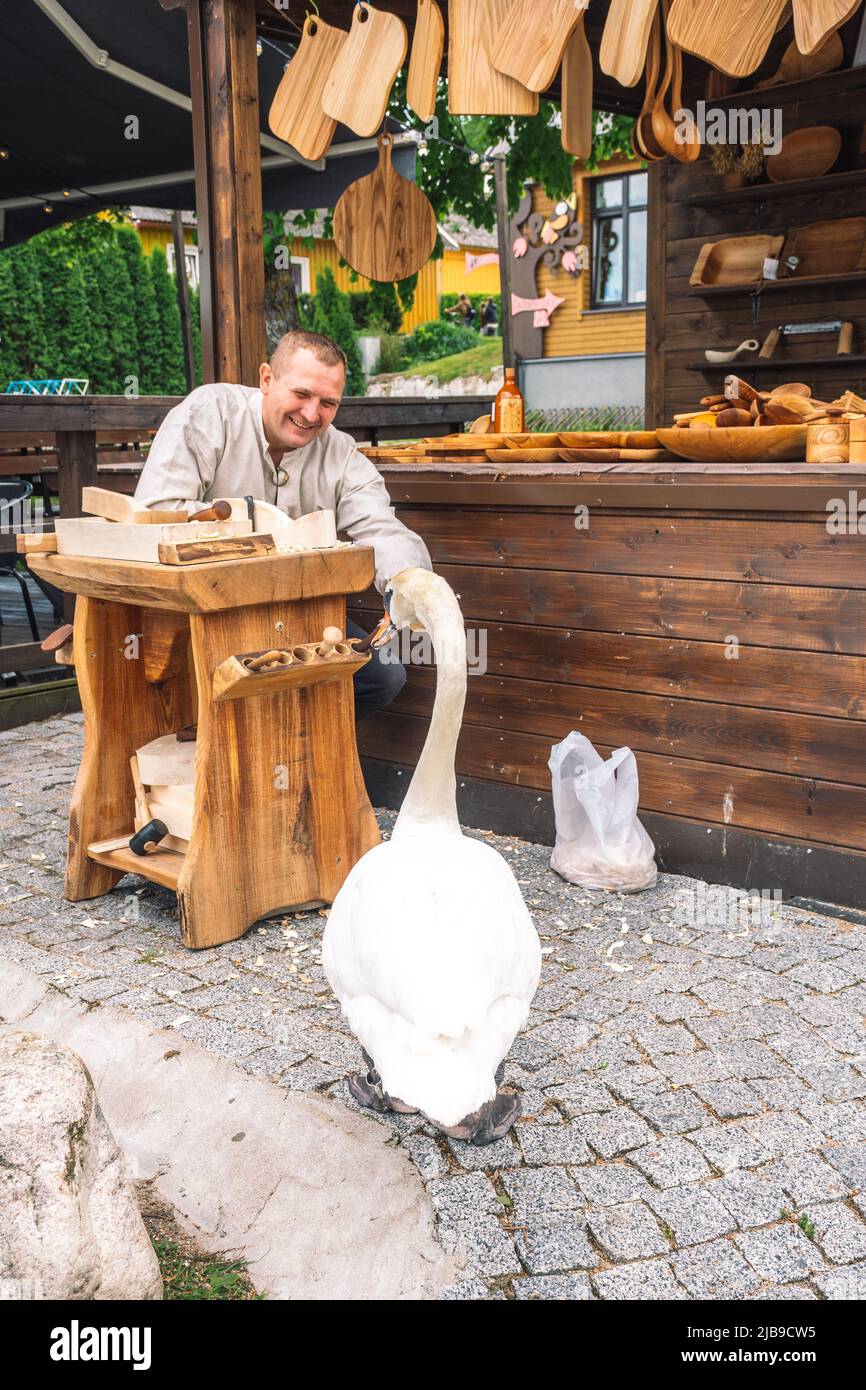 Lithuanian craftsman in traditional costumes carving wood and selling ...