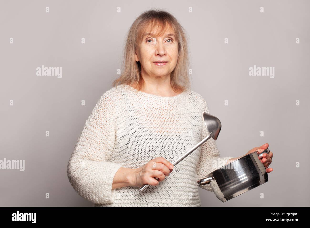 Cute mature woman 60s with spoon soup ladle and saucepan in her hands ...