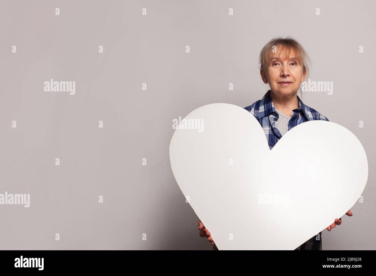 Attractive woman with empty white heart banner on grey studio ...