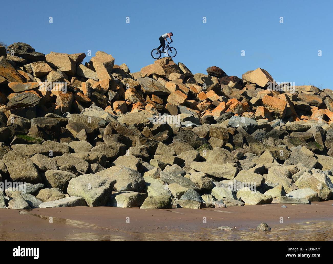 An acrobatic cyclist performing stunts on multi-coloured rock armour ...