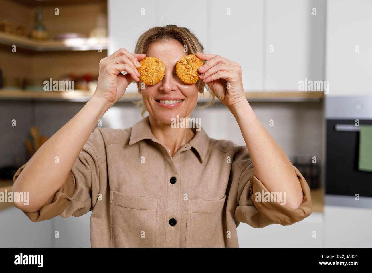 Portrait of mature woman who covers eyes with delicious cookies at the ...
