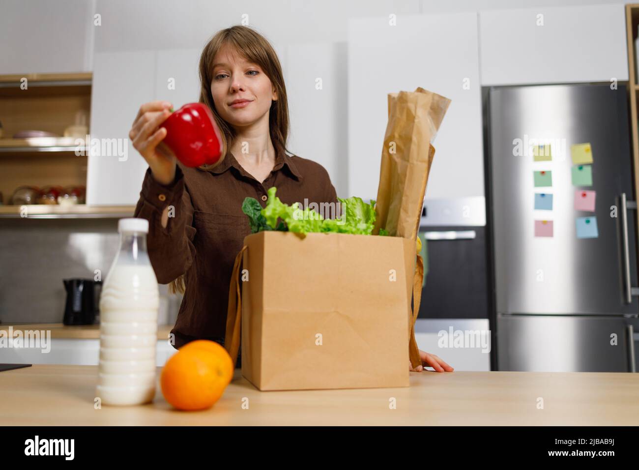 Woman unpacking vegetables and other food from paper grocery bag into ...