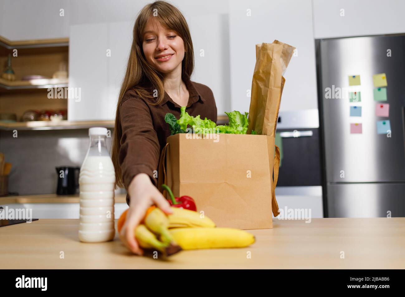 Girl unpacking food from a paper grocery bag in the kitchen Stock Photo ...