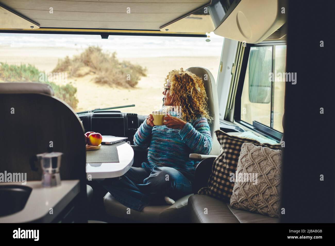 Serene adult woman admiring nature beach sitting inside a modern camper ...