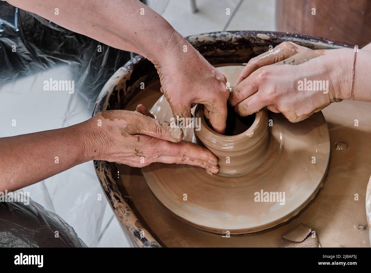 Hands of senior woman and girl sculpting clay vase on potter's wheel at ...