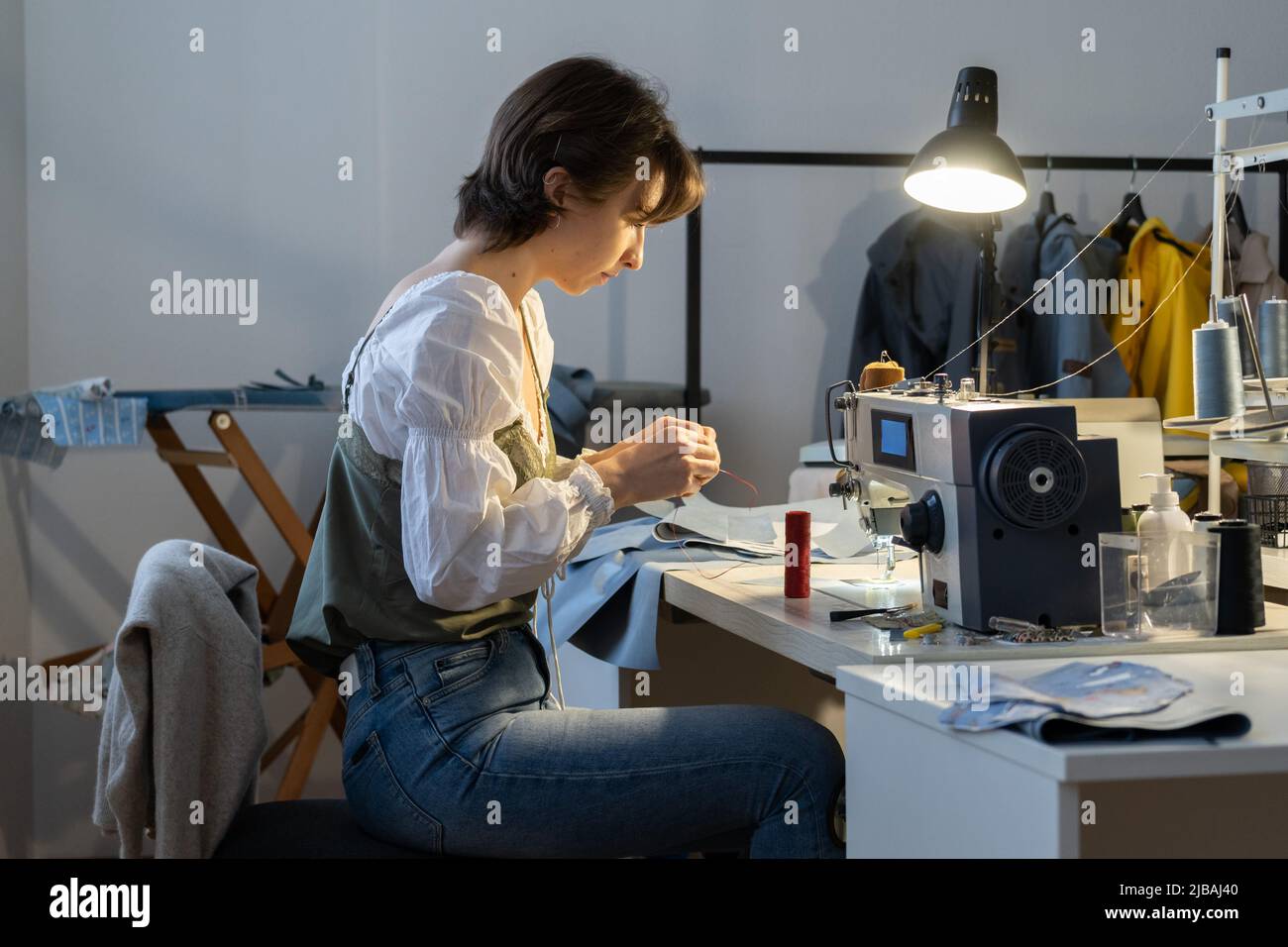 Young female seamstress sew on sewing machine, tailor sit at workplace ...
