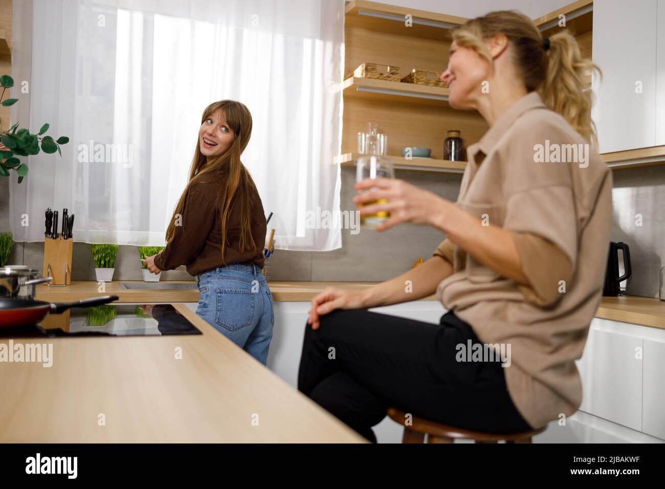 Nice girl washing dishes while her mother is relaxing sitting at the ...