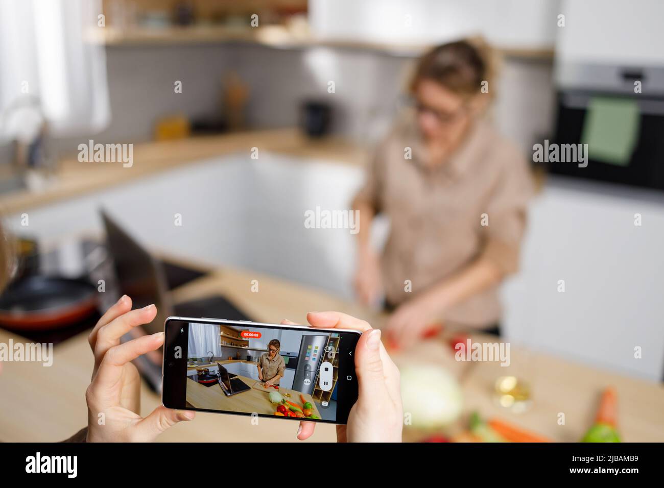 Daughter with smartphone filming her mother while cooking in the ...
