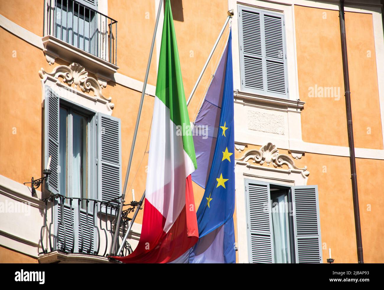 Italian flag and European flag waving in the air hanging on a balkony ...