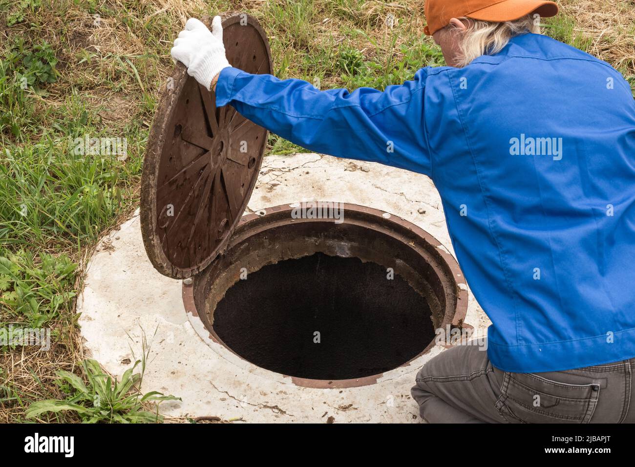 A working plumber opens a sewer hatch. Maintenance of septic tanks and ...