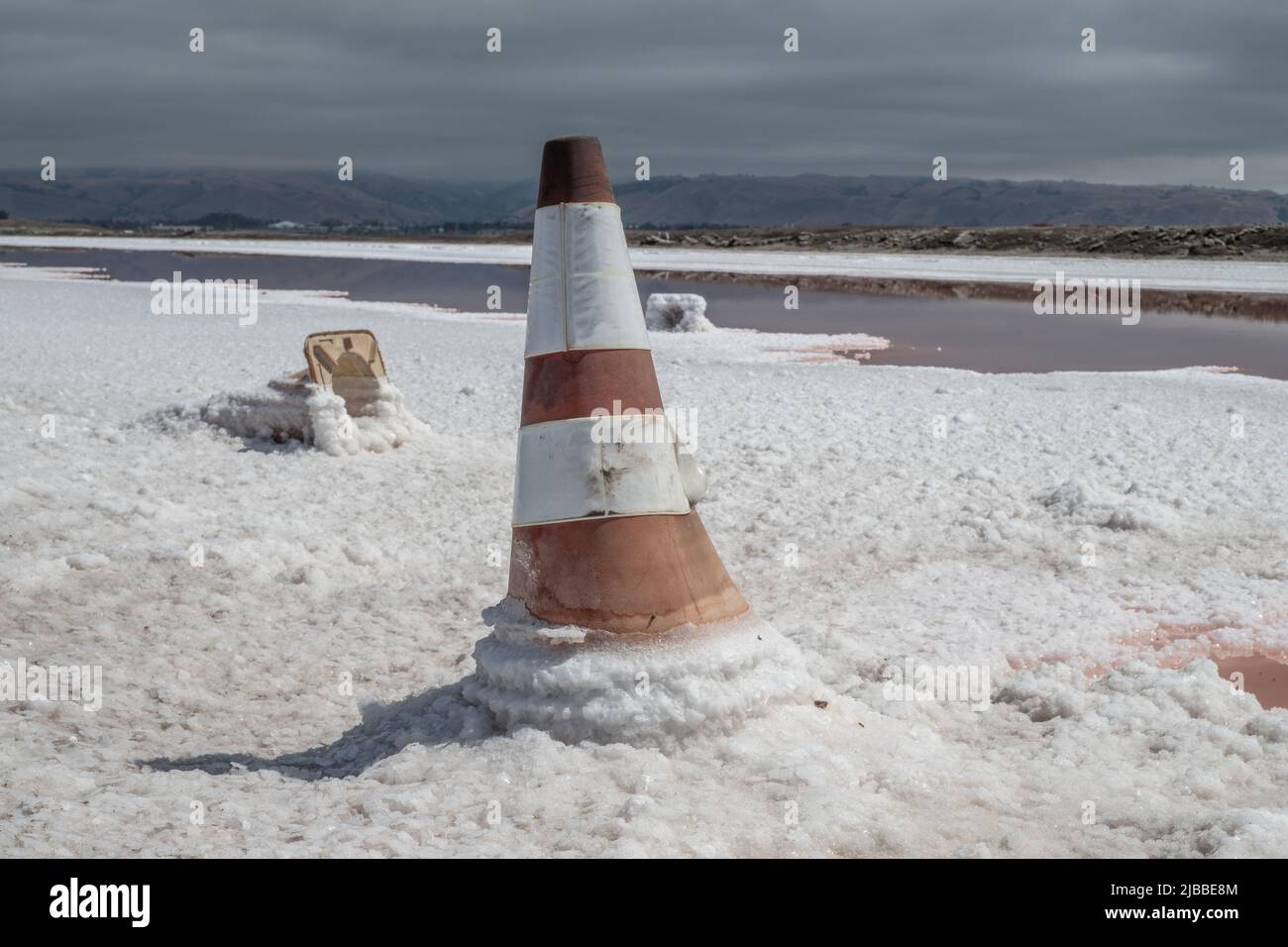 A traffic cone covered in salt crystals at the edge of saltpond where ...