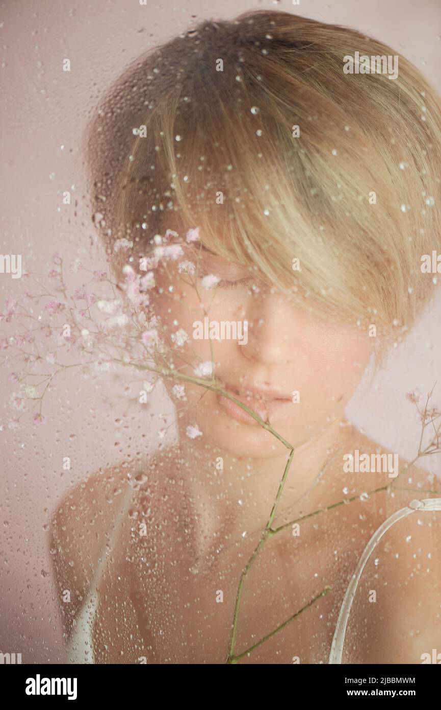 A gentle girl on a pink background, behind fogged glass. Femininity and ...