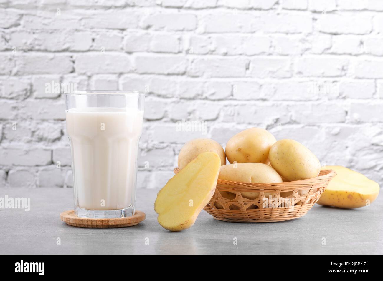 Vegan potato milk in a glass and potato tubers on grey stone table ...