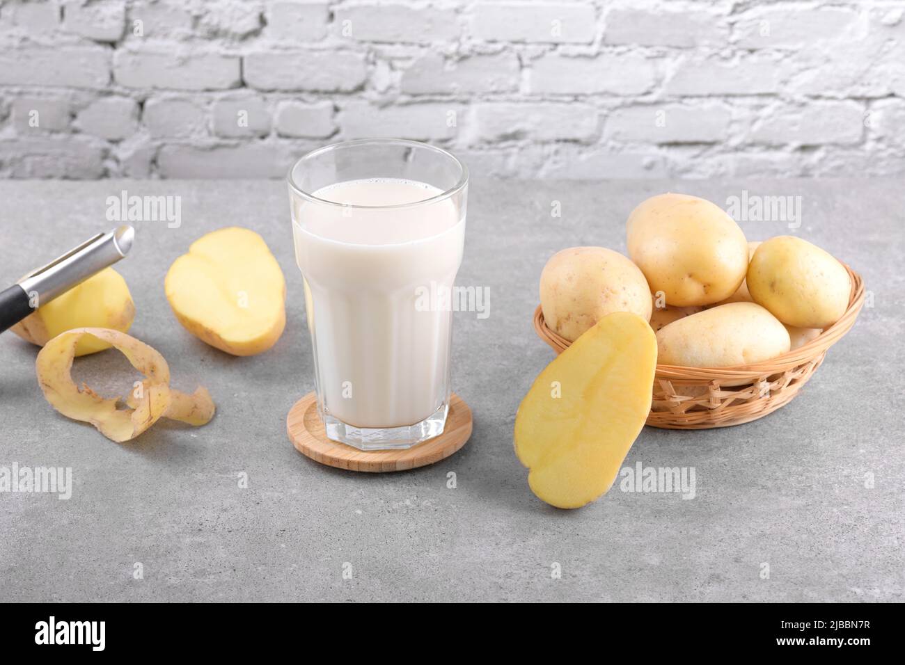 Vegan potato milk in a glass and potato tubers on grey stone table ...