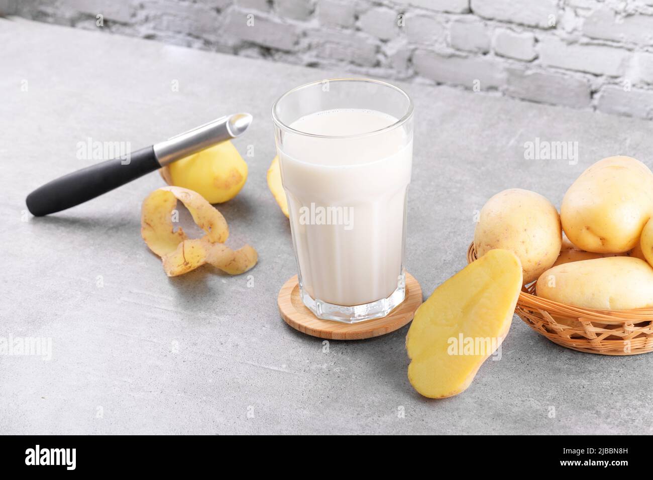 Vegan potato milk in a glass and potato tubers on grey stone table ...
