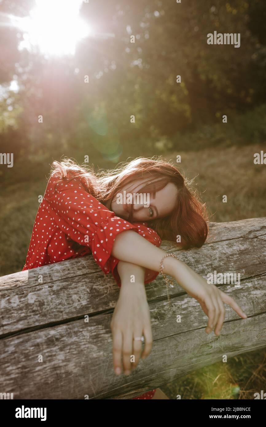 Young woman with red long curly thick hair lying down on a dry fallen ...