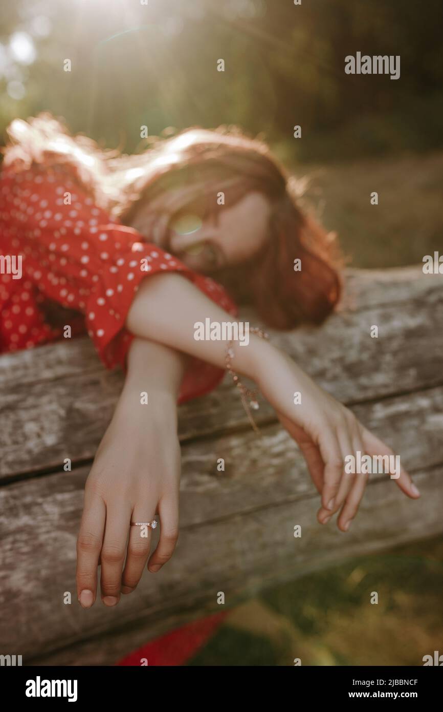 Young woman with red long curly thick hair lying down on a dry fallen ...