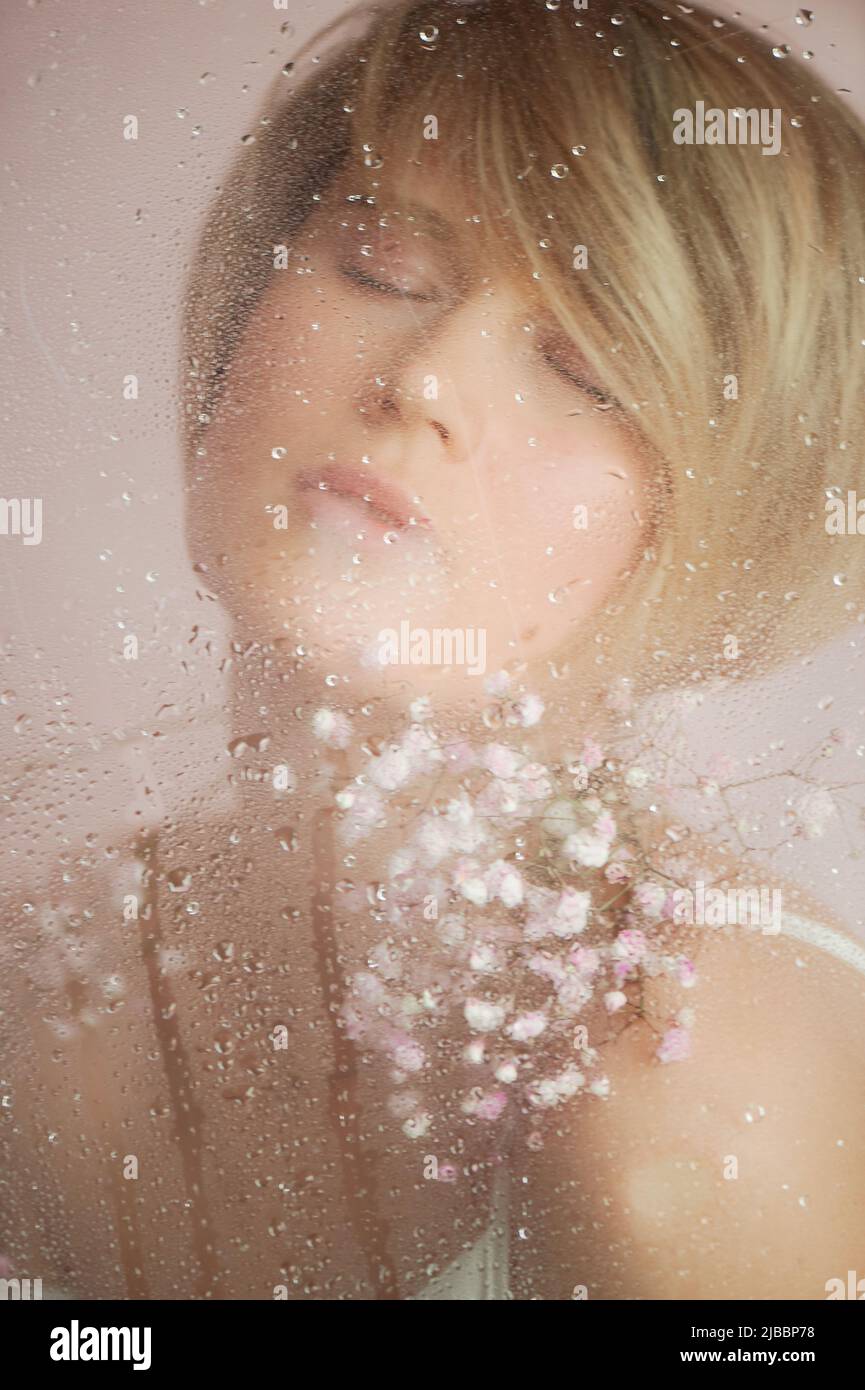 A girl with flowers behind wet glass. Nega and enjoyment of life. Eyes ...