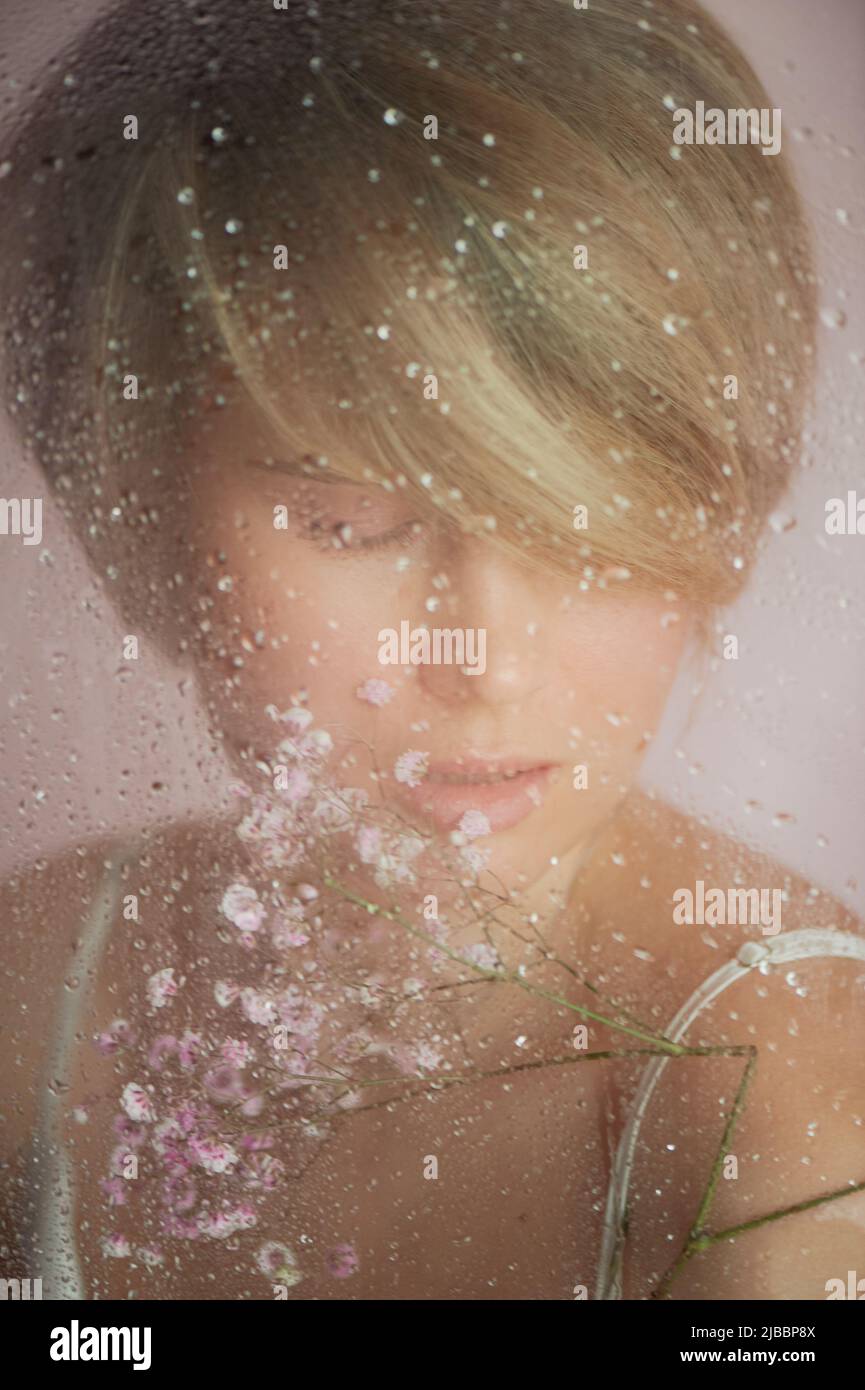 A girl with flowers behind wet glass. Nega and enjoyment of life. Eyes ...