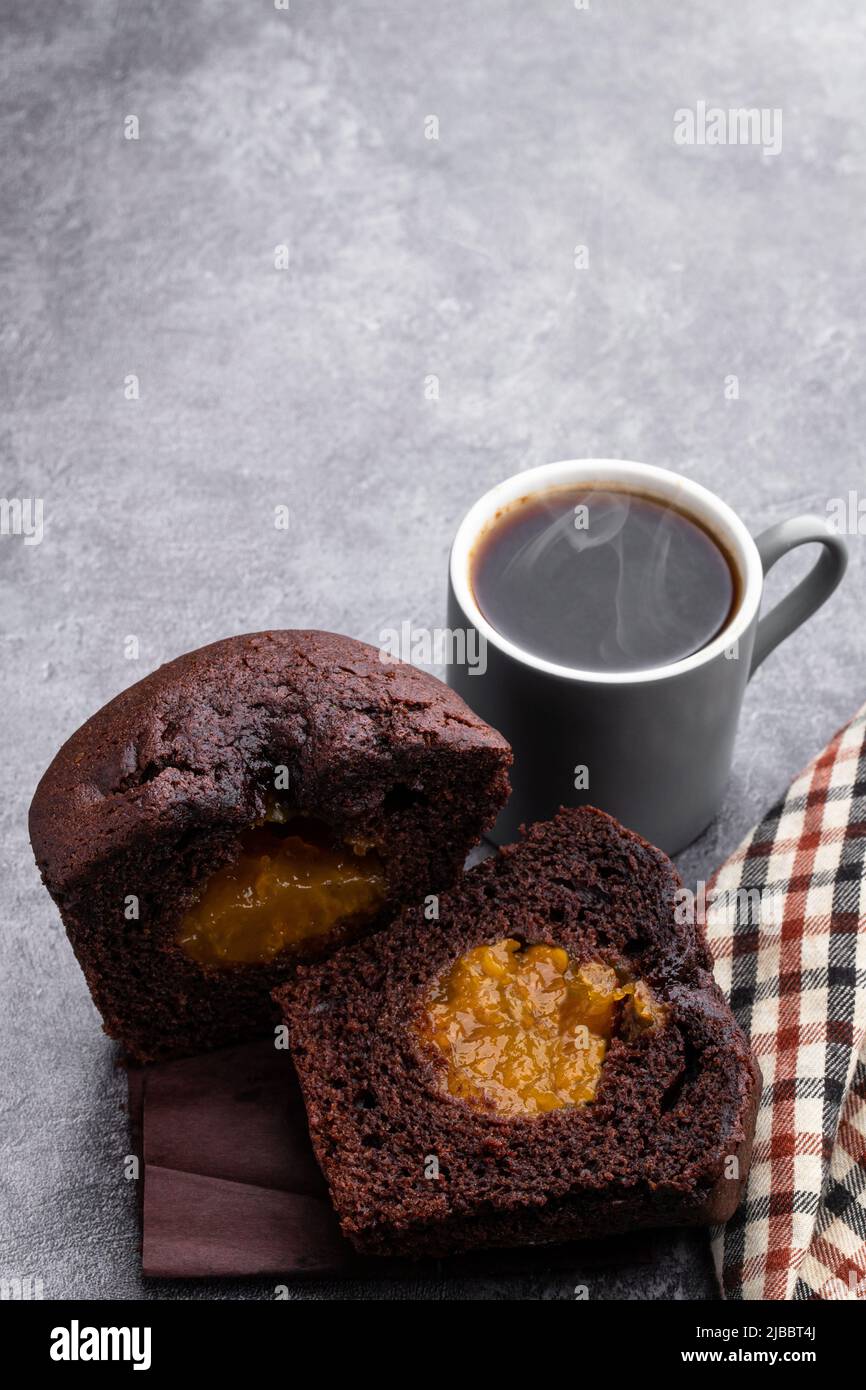 Dark chocolate muffin stuffed with yellow jam and cup of coffee on gray ...