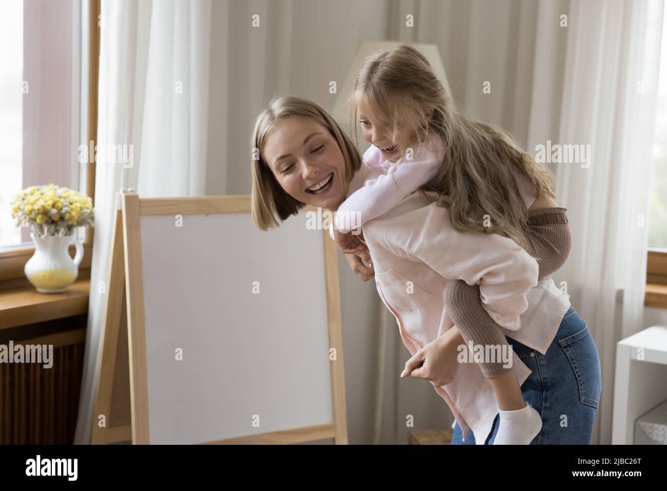 Cute little daughter piggyback mommy enjoy playtime together at home ...