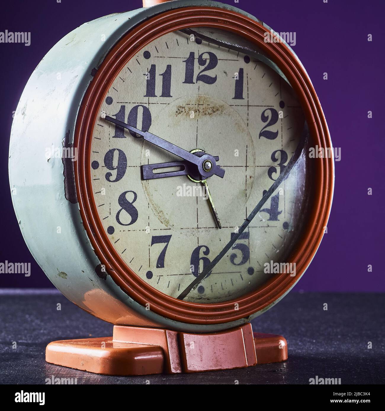 Dirty old broken rusty alarm clock. Broken dial. Red body violet ...