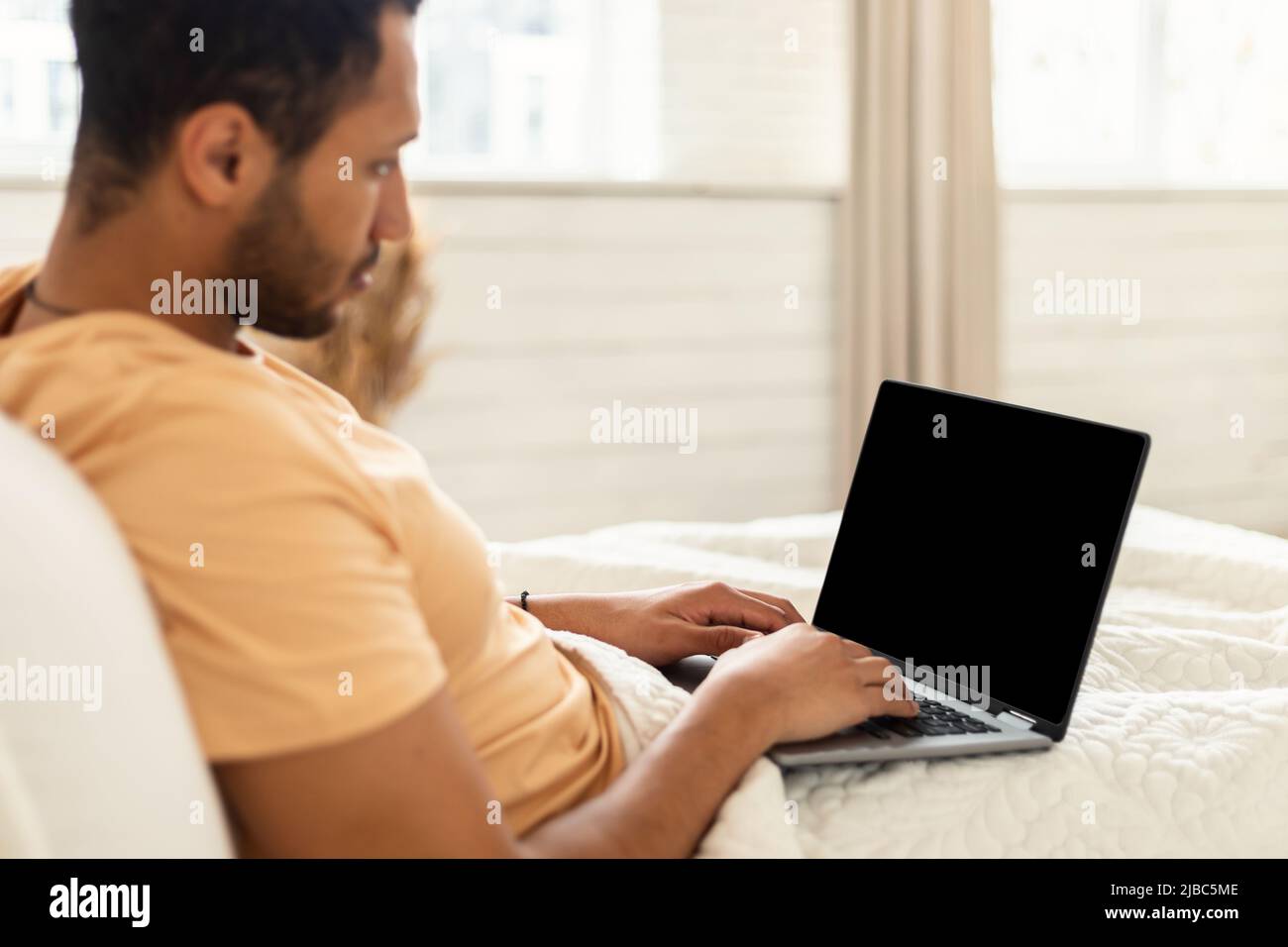 Arabic Guy Using Laptop With Blank Screen In Bedroom Stock Photo - Alamy