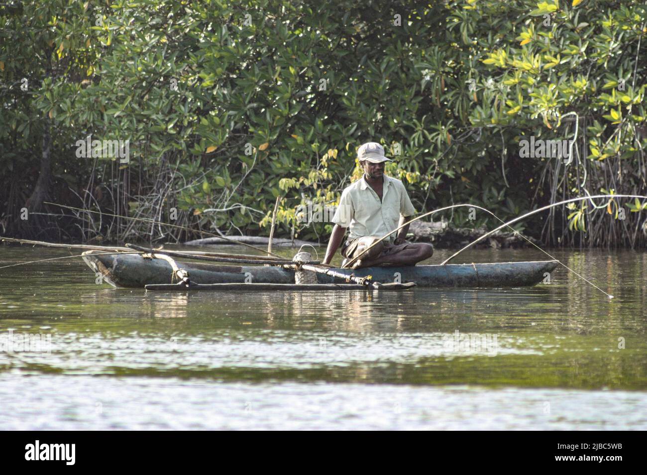 A Sri Lankan fisherman on a primitive boat fishing several lines at ...