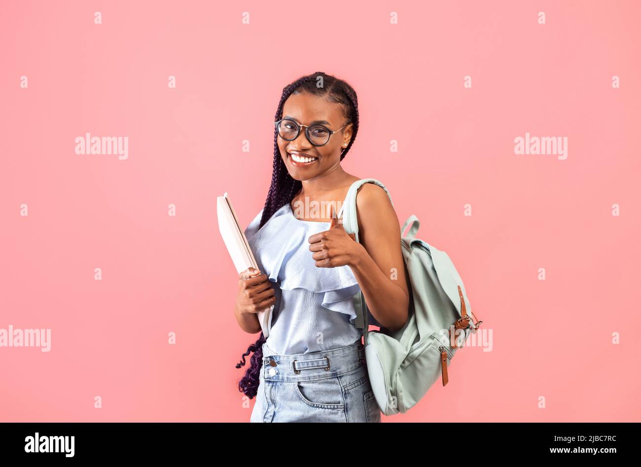 Young black female student with books and backpack showing thumb up ...