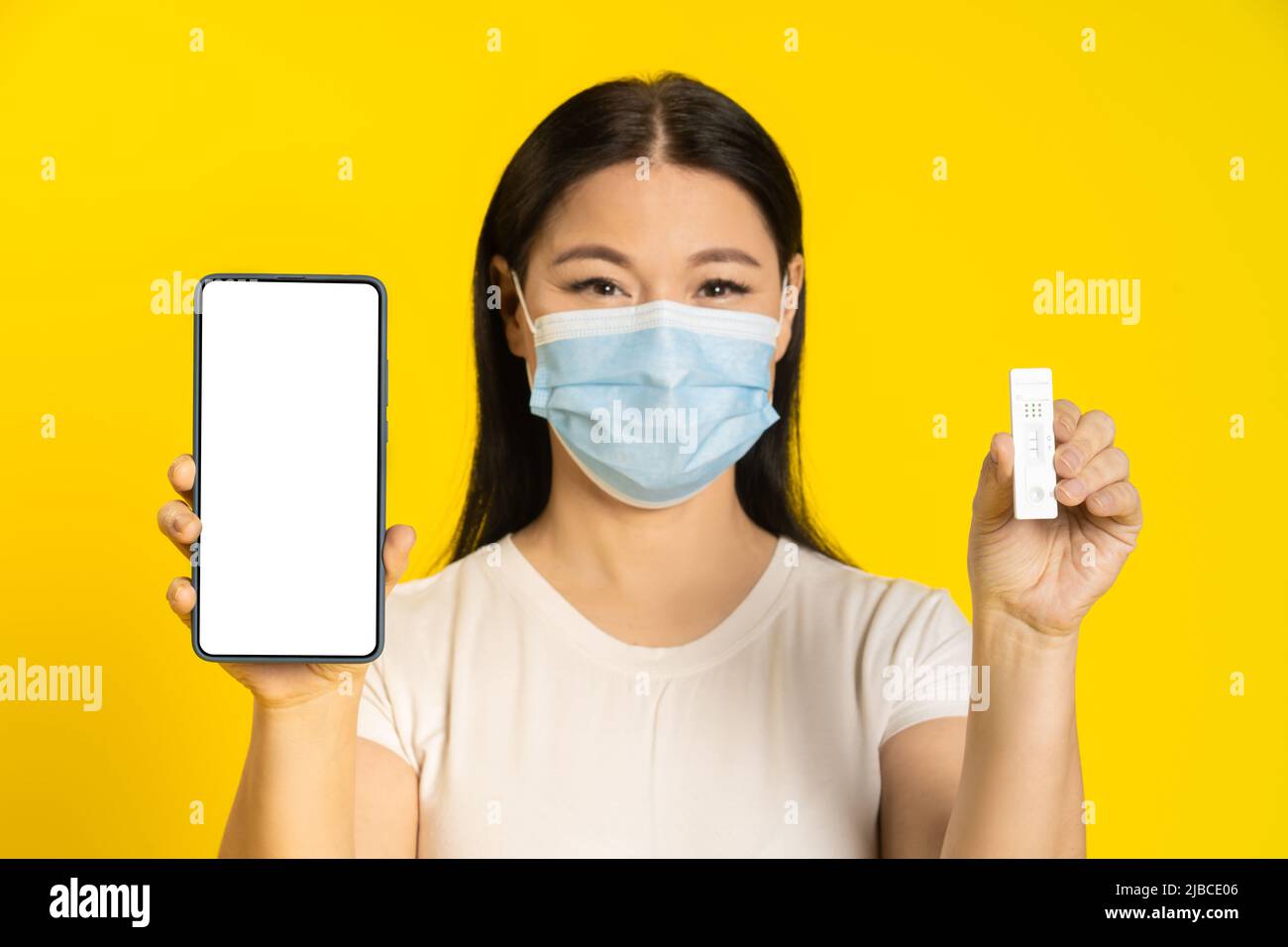 Happy asian woman wearing medical face mask, holding smartphone and ...