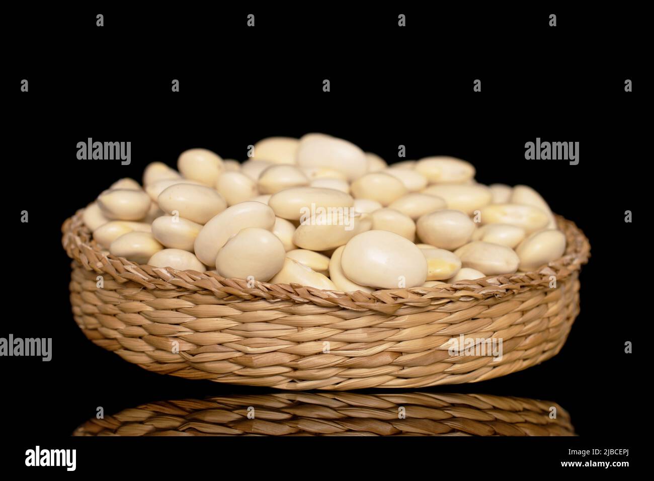 Uncooked white beans in a straw plate, close-up, isolated on a black ...