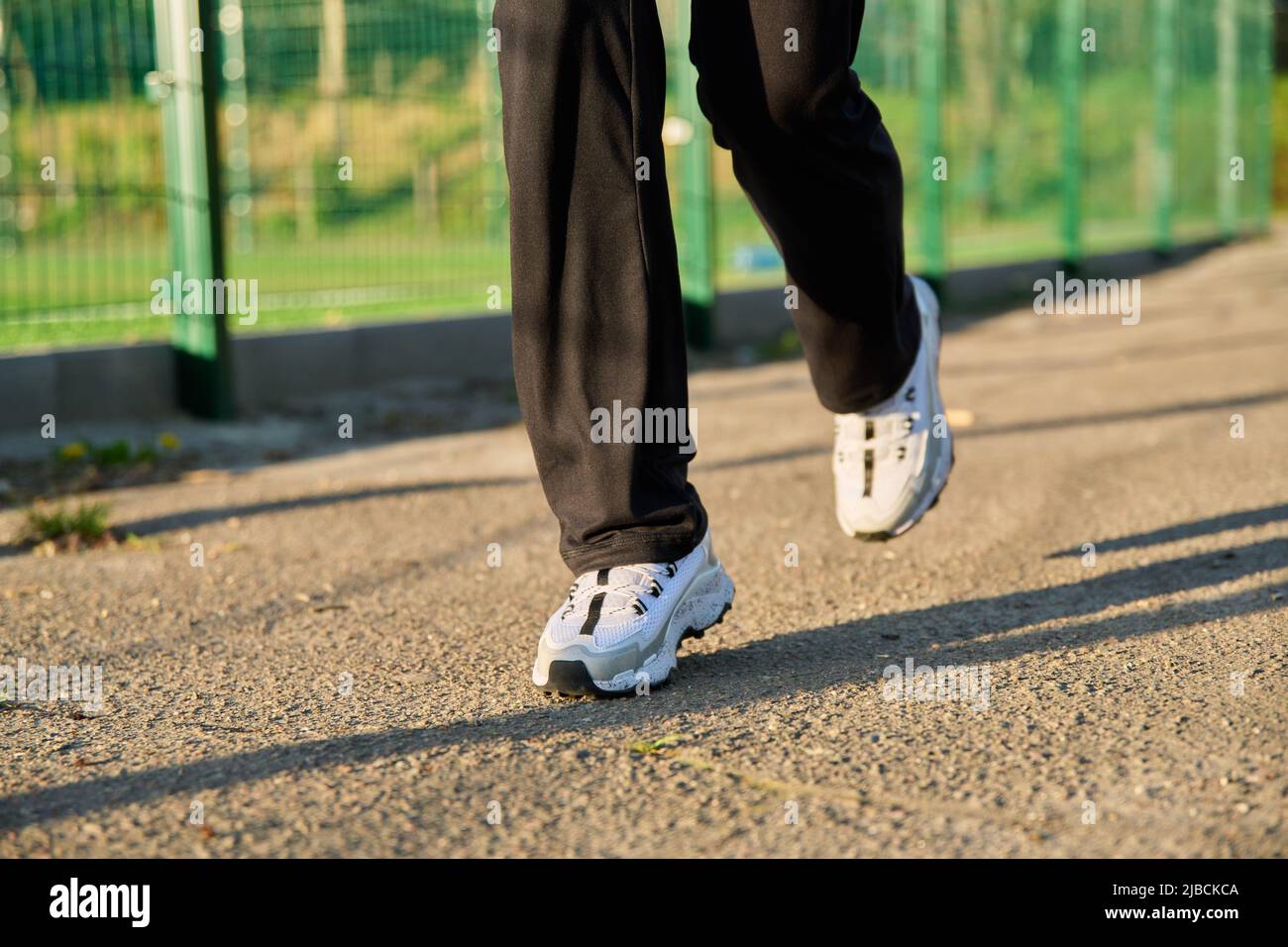 Close-up of female legs in white sneakers running along the road near ... Close-up of female legs in white sneakers running along the road near ...