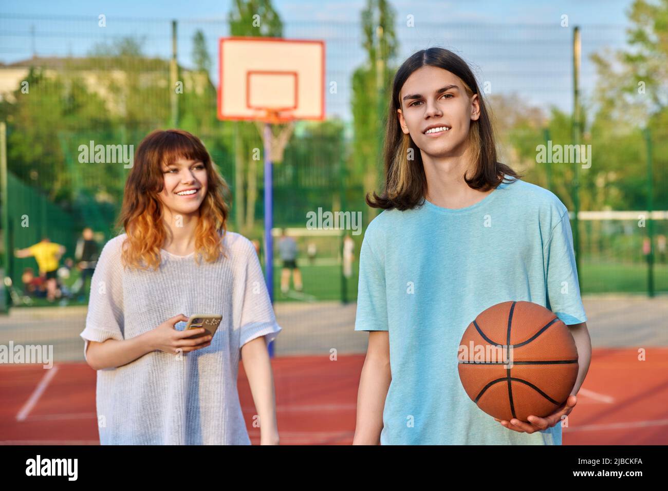 Portrait of young guy playing basketball on an outdoor game court, girl ...