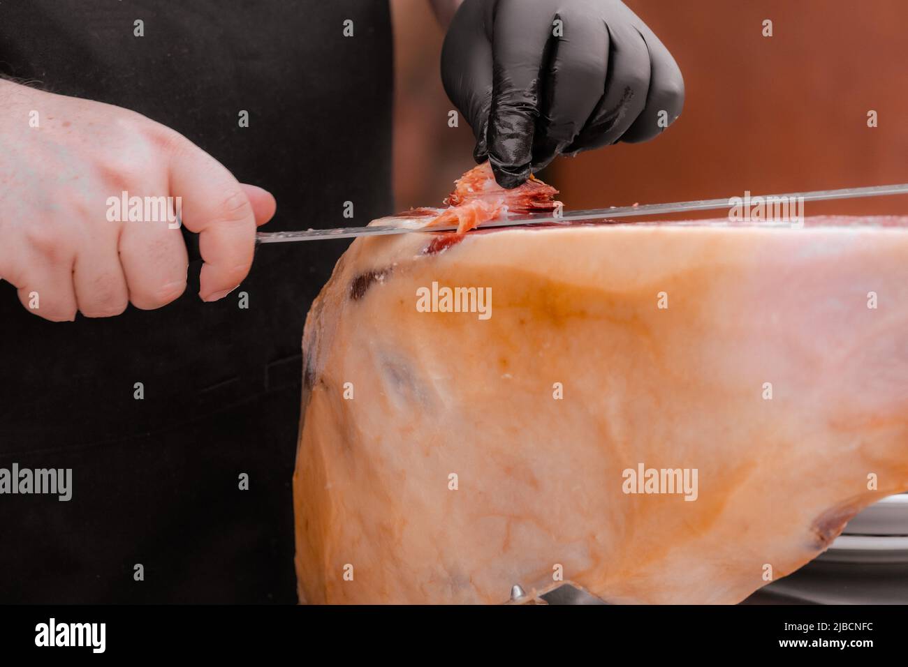Professional Iberico or Serrano ham cutter is cutting a sliced pork leg ...
